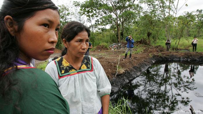 Cofán women stand before an open well contaminated with petroleum in ...